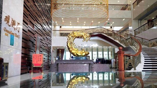 Um interior moderno com uma escadaria central, uma escultura dourada decorativa e uma superfície de vidro refletora.