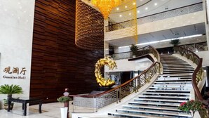 Um saguão de hotel em vários níveis, com uma escadaria imponente, uma grande escultura dourada e uma placa com a inscrição 'Guanglan Hall'.