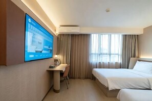 Quarto de hotel com cama, escrivaninha, cadeira, televisão na parede e janela com cortinas.
