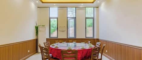 Uma sala de conferências com uma mesa redonda, cadeiras de madeira e toalha de mesa vermelha.