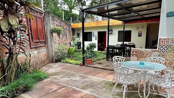 Uma área de pátio coberta com mesa e cadeiras, cercada por vasos de plantas e uma parede de tijolos.