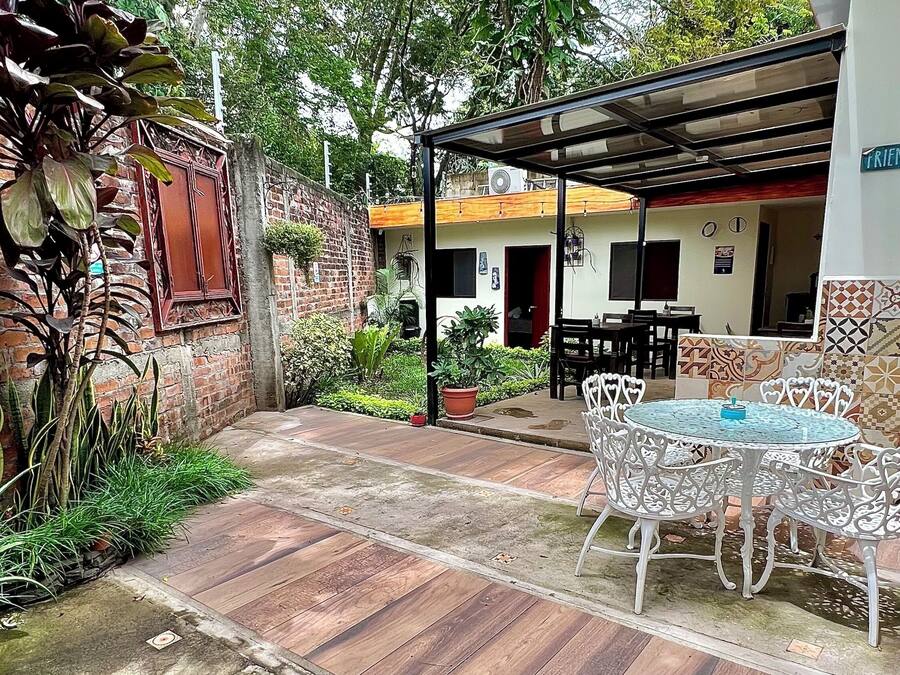 Uma área de pátio coberta com mesa e cadeiras, cercada por vasos de plantas e uma parede de tijolos.