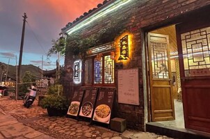 Edifício tradicional com porta de madeira, sinalização e um quadro de menu do lado de fora, além de entrada com piso de pedra.