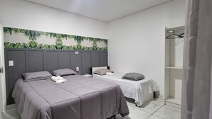 Quarto com duas camas, cabeceira cinza, mesa de cabeceira pequena e planta fixada na parede.