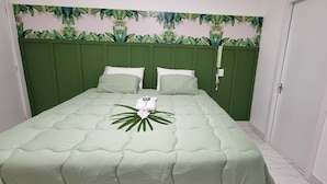 Uma cama com cabeceira verde, duas almofadas e um arranjo decorativo de plantas.