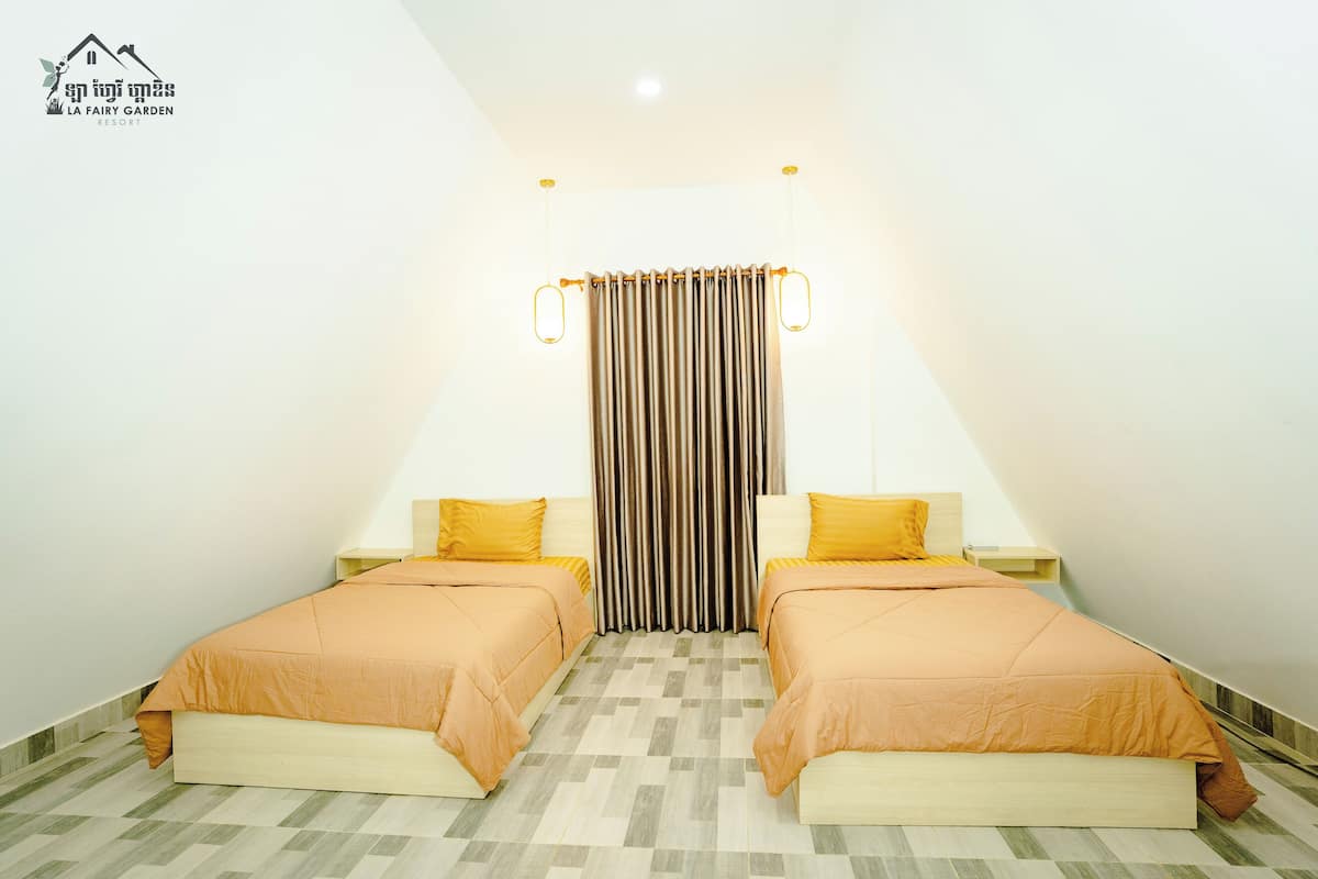 Quarto com duas camas, cortina e luminária.