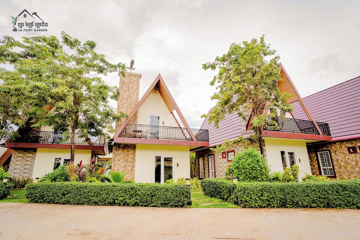 Uma casa de dois andares com fachada de pedra, telhado vermelho e varanda com guarda-corpo preto.