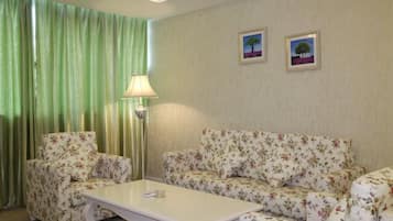 Sala de estar com sofá floral, mesa de centro branca e luminária. Há duas quadros nas paredes.
