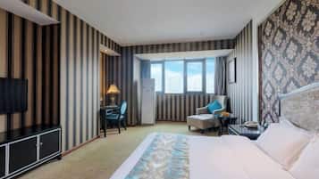 Quarto de hotel com uma cama grande, escrivaninha, cadeira, televisão e janela com vista.