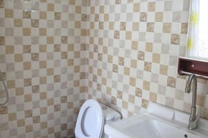 Casa de banho com azulejos quadriculados na parede, sanita branca e lavatório com torneira.