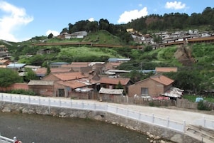 Uma aldeia à beira-rio com casas tradicionais, uma ponte branca e um muro de pedra.