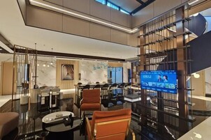 Um lobby amplo com pé-direito alto, uma tela grande exibindo informações e um design de interiores moderno.