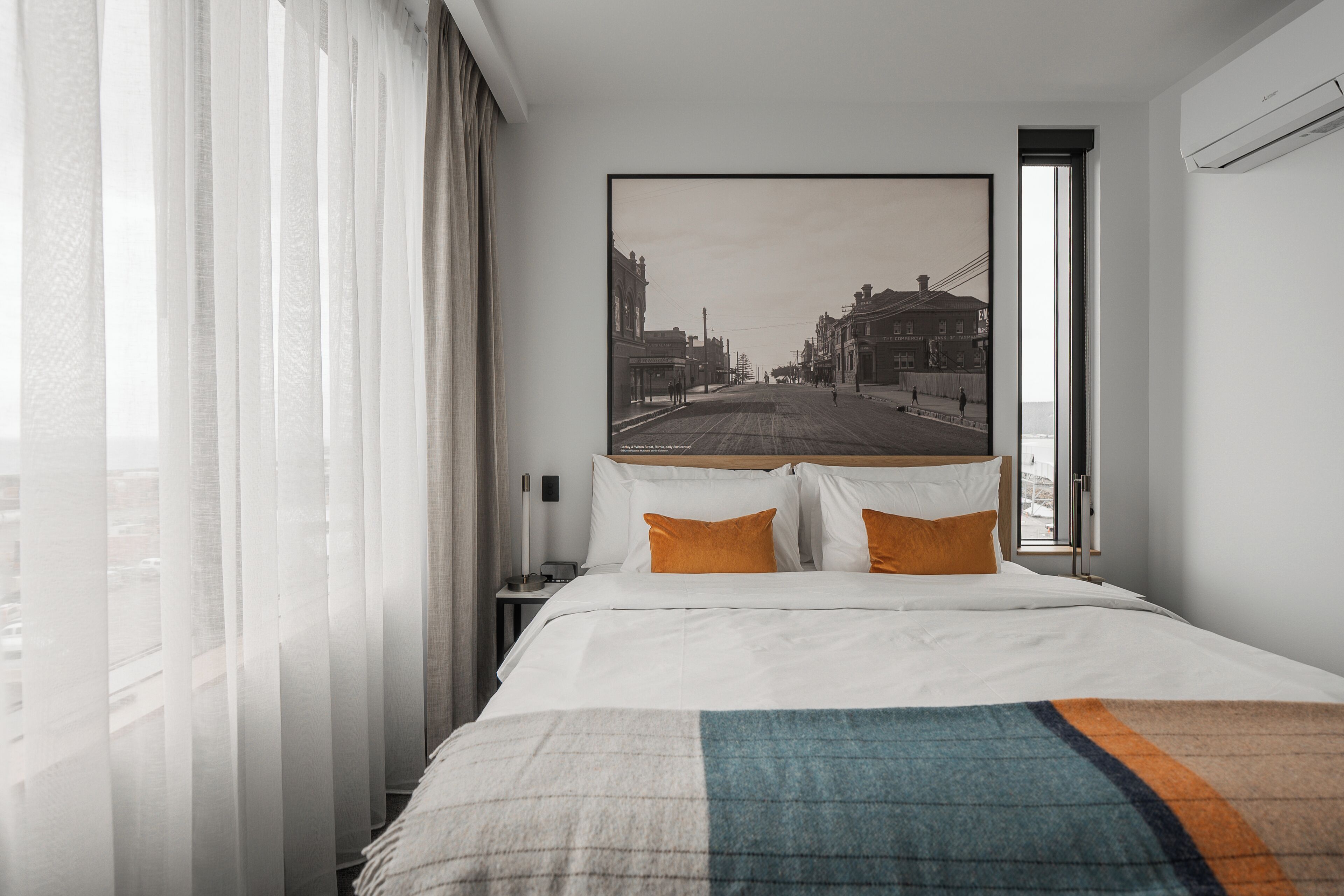 Quarto de hotel com cama grande, roupa de cama branca e vista para a rua pela janela.
