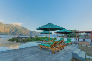 Uma área na piscina com espreguiçadeiras e guarda-sóis, com vista para um lago e montanhas.