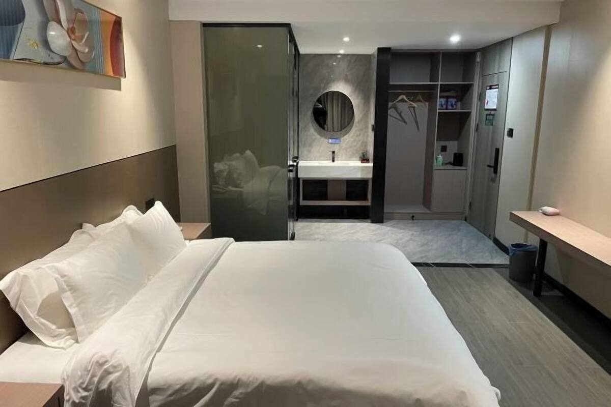 Quarto de hotel com cama, mesa de cabeceira, espelho, guarda-roupa e banheiro com pia e espelho.
