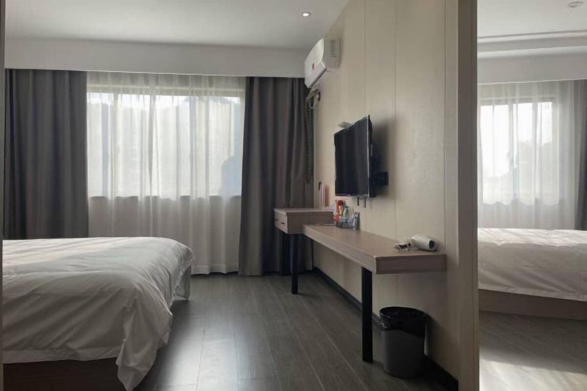 Quarto de hotel com duas camas, uma escrivaninha, televisão e janela com cortinas.