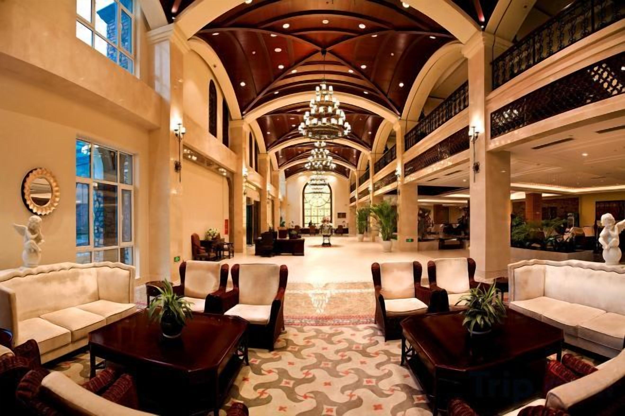 Um hall amplo, com pé direito alto, um imponente candelabro e uma área de estar central com sofás e poltronas.