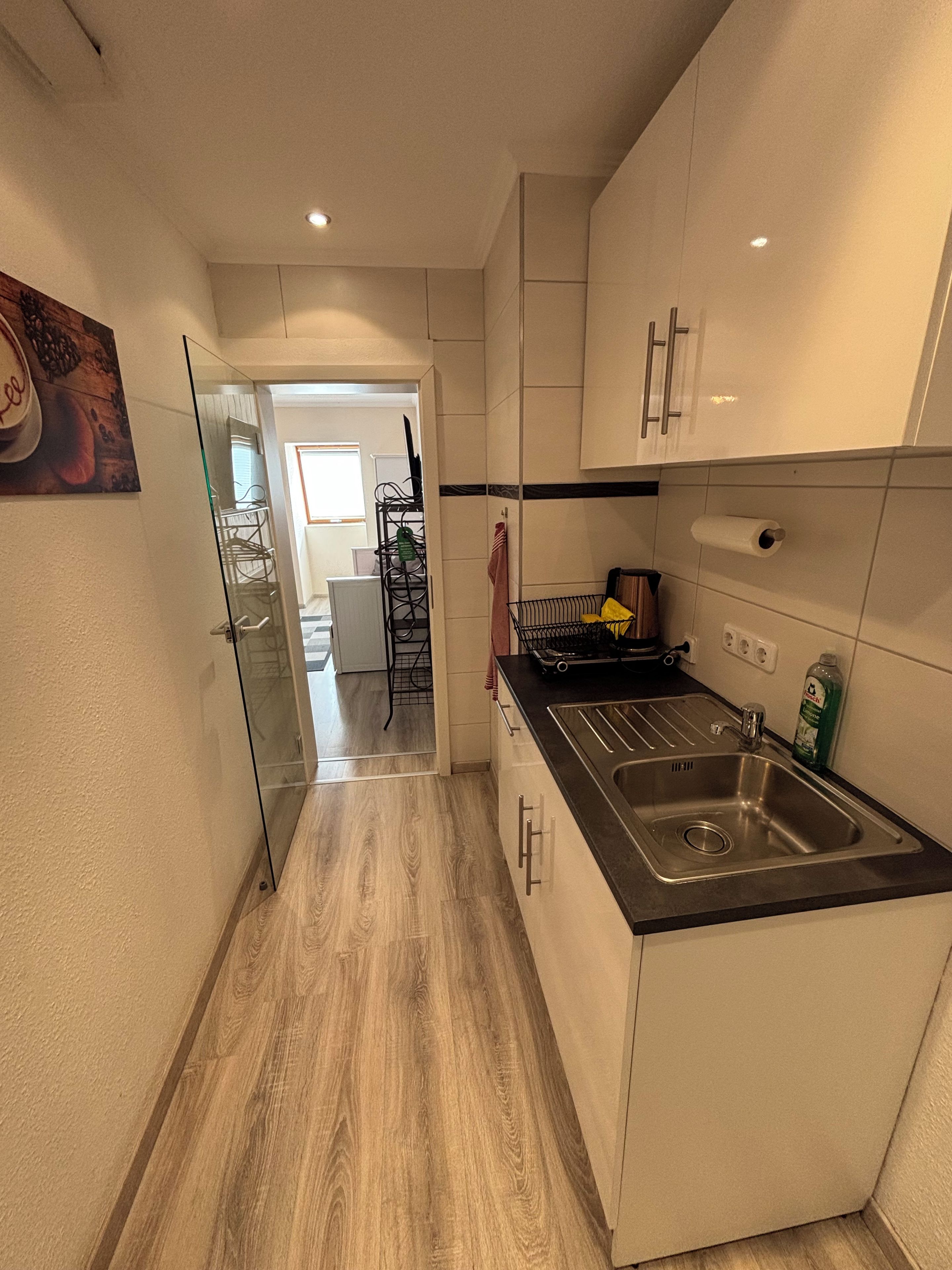 Cozinha moderna com pia de aço inoxidável, piso de madeira e armários brancos.