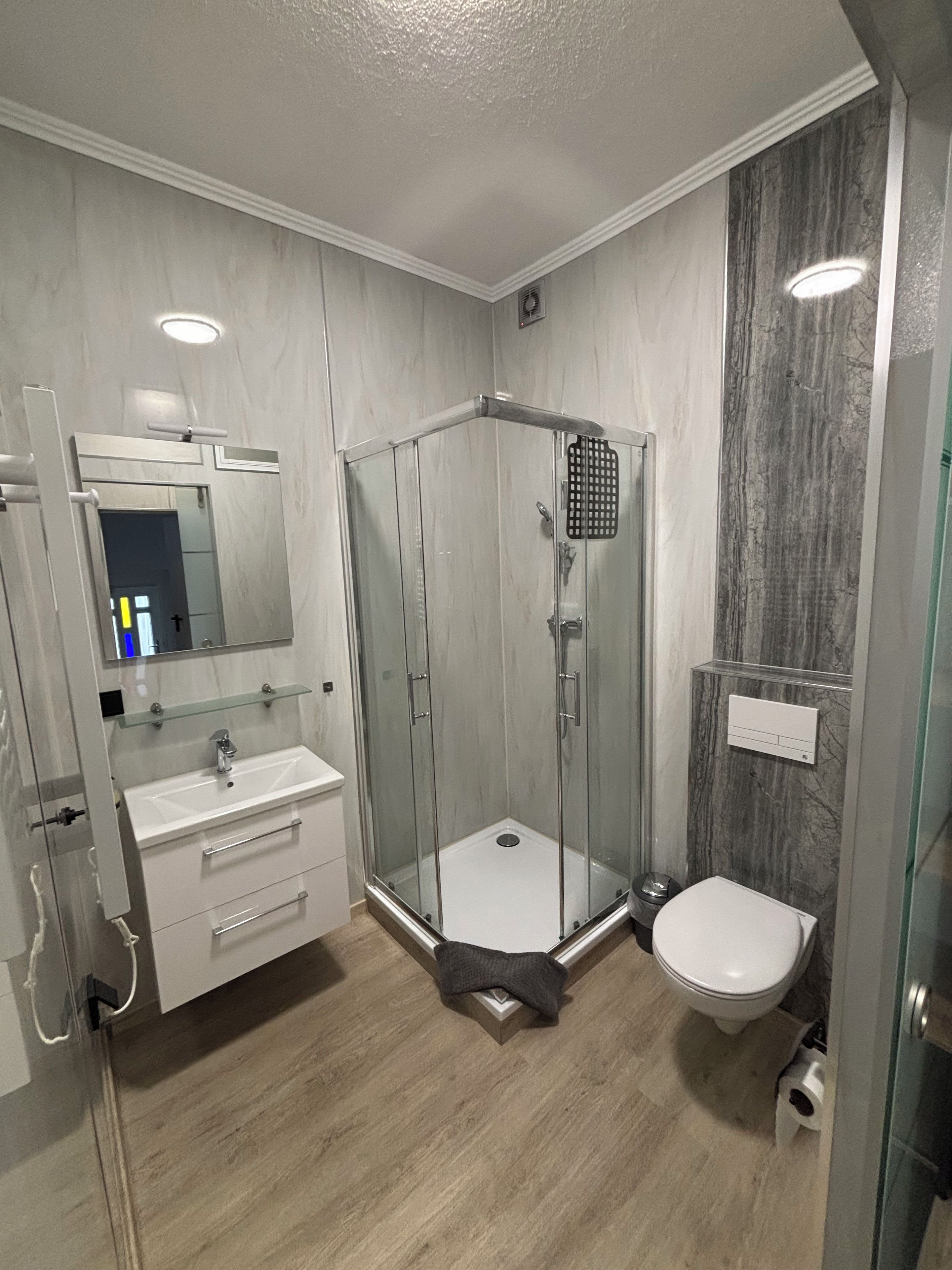 Casa de banho moderna com chuveiro em cabine de vidro, lavatório branco e sanita.