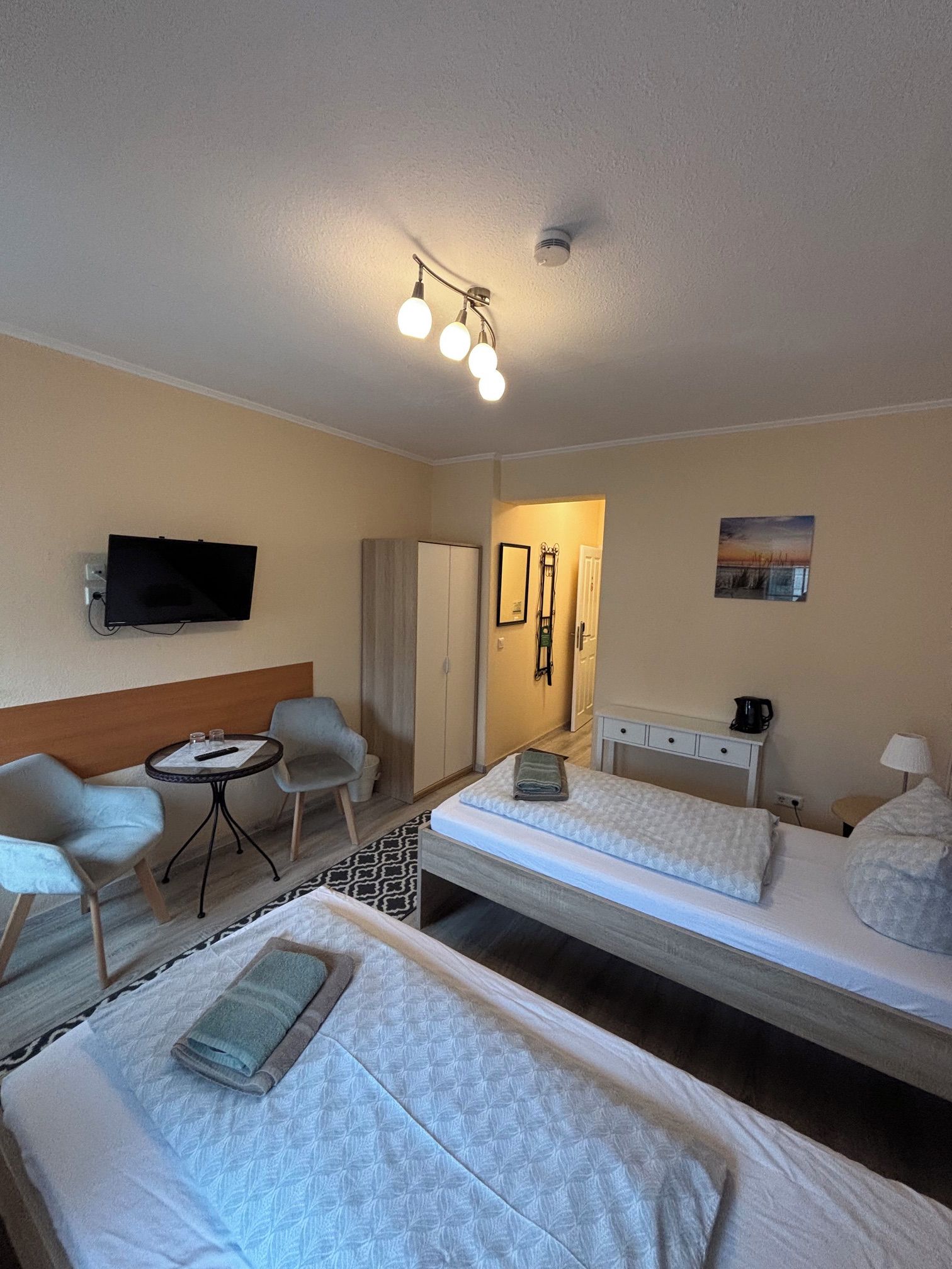 Quarto de hotel com duas camas, televisão, escrivaninha, cadeira e mesa pequena.
