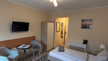 Quarto de hotel com duas camas, televisão, escrivaninha, cadeira e mesa pequena.