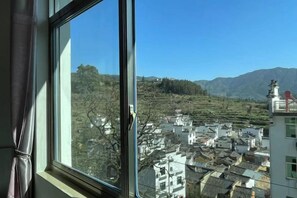 Vista pela janela de uma cidade, com edifícios e uma cordilheira ao fundo.