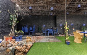 Um pátio externo com cadeiras azuis, uma mesa e plantas em vasos.
