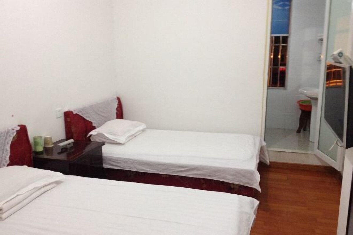Quarto de hotel com duas camas de solteiro, uma pequena mesa com produtos de higiene pessoal, e vista para o exterior por uma porta de vidro.