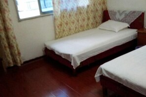 Quarto pequeno com duas camas de solteiro, janela com cortinas e piso de madeira.