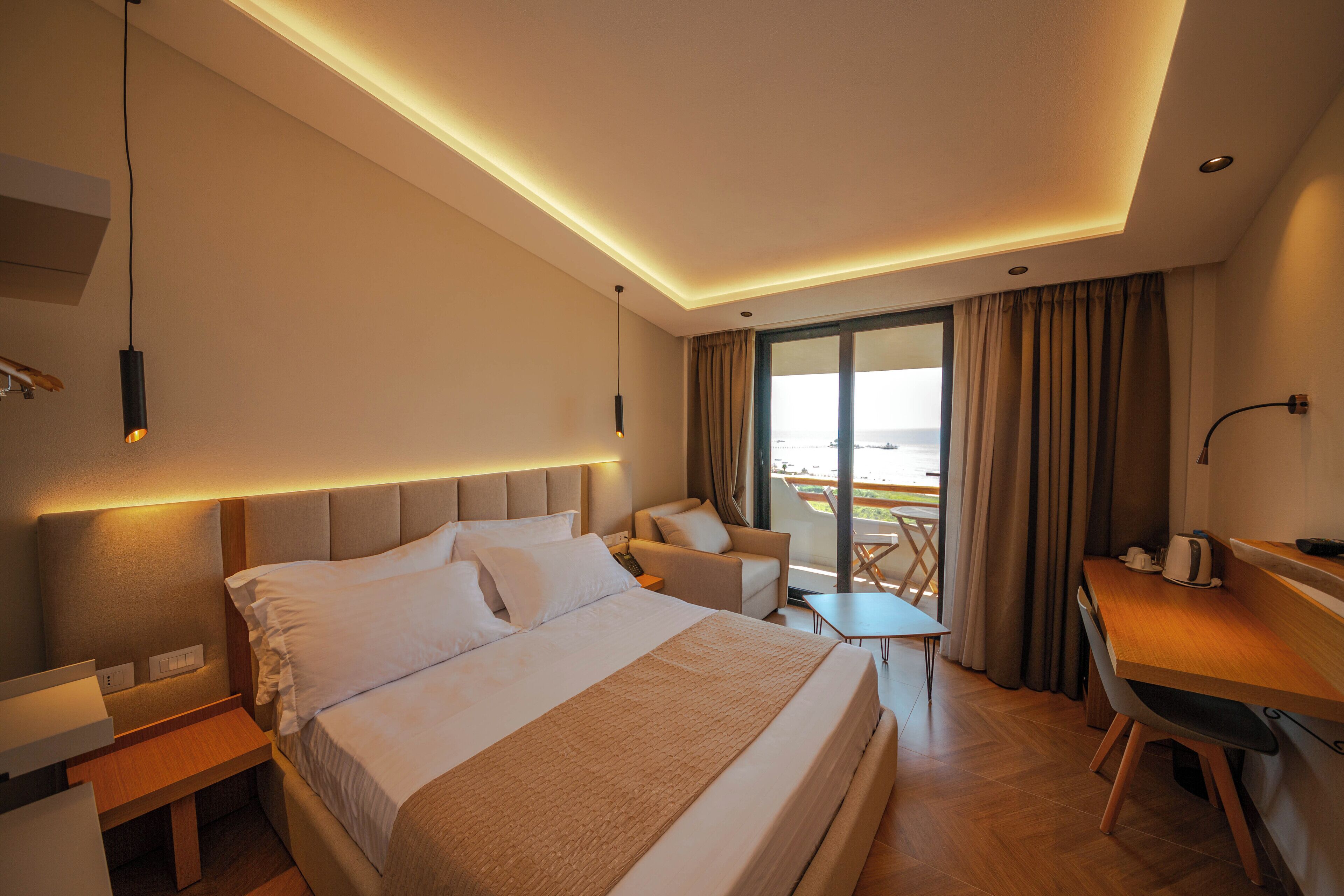 Quarto de hotel moderno com uma cama grande, uma mesa de trabalho e uma varanda com vista.