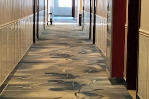 Corredor com piso estampado, que leva a uma vista distante através de uma porta de vidro.