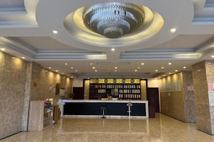 Um saguão de hotel com balcão de recepção, um lustre e uma parede de garrafas de bebidas alcoólicas.