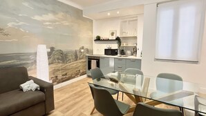 Uma sala de estar moderna com uma mesa de jantar de vidro, cadeiras cinzas e um sofá marrom.