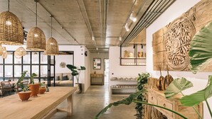 Um interior moderno com uma longa mesa de madeira, luminárias de vime suspensas e grandes folhas decorativas.
