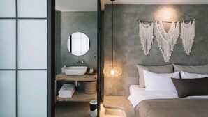Uma casa de banho moderna com um espelho redondo, lavatório branco e cama com cabeceira em macramé.