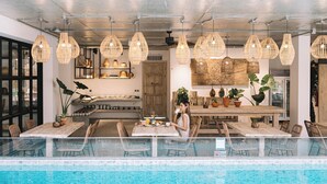 Um restaurante com área de piscina, com luminárias pendentes de vime, mesas e cadeiras de madeira.