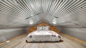 Um quarto com teto inclinado, piso de madeira e cama com colcha florida.