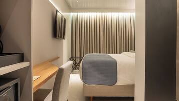 Quarto de hotel moderno com cama, escrivaninha, cadeira, televisão e minibar.