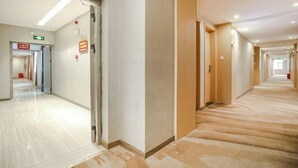 Corredor de hotel com piso lustroso, parede de madeira e porta que dá para outro quarto.