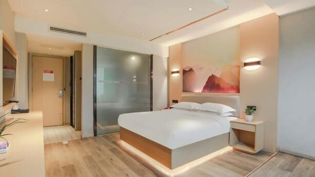 Quarto moderno com uma cama grande, mesas de cabeceira, um criado-mudo, uma luminária na parede e uma porta com uma placa.