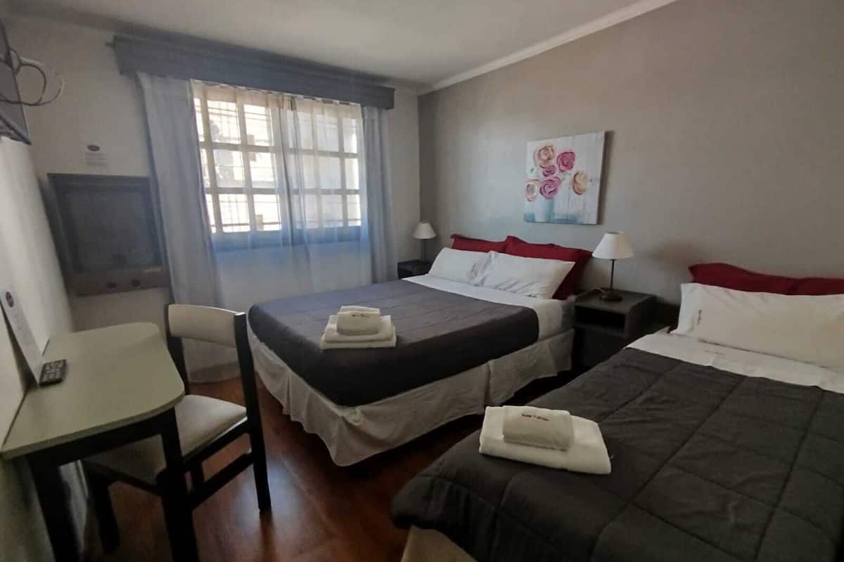 Quarto de hotel com duas camas, uma escrivaninha e uma televisão.