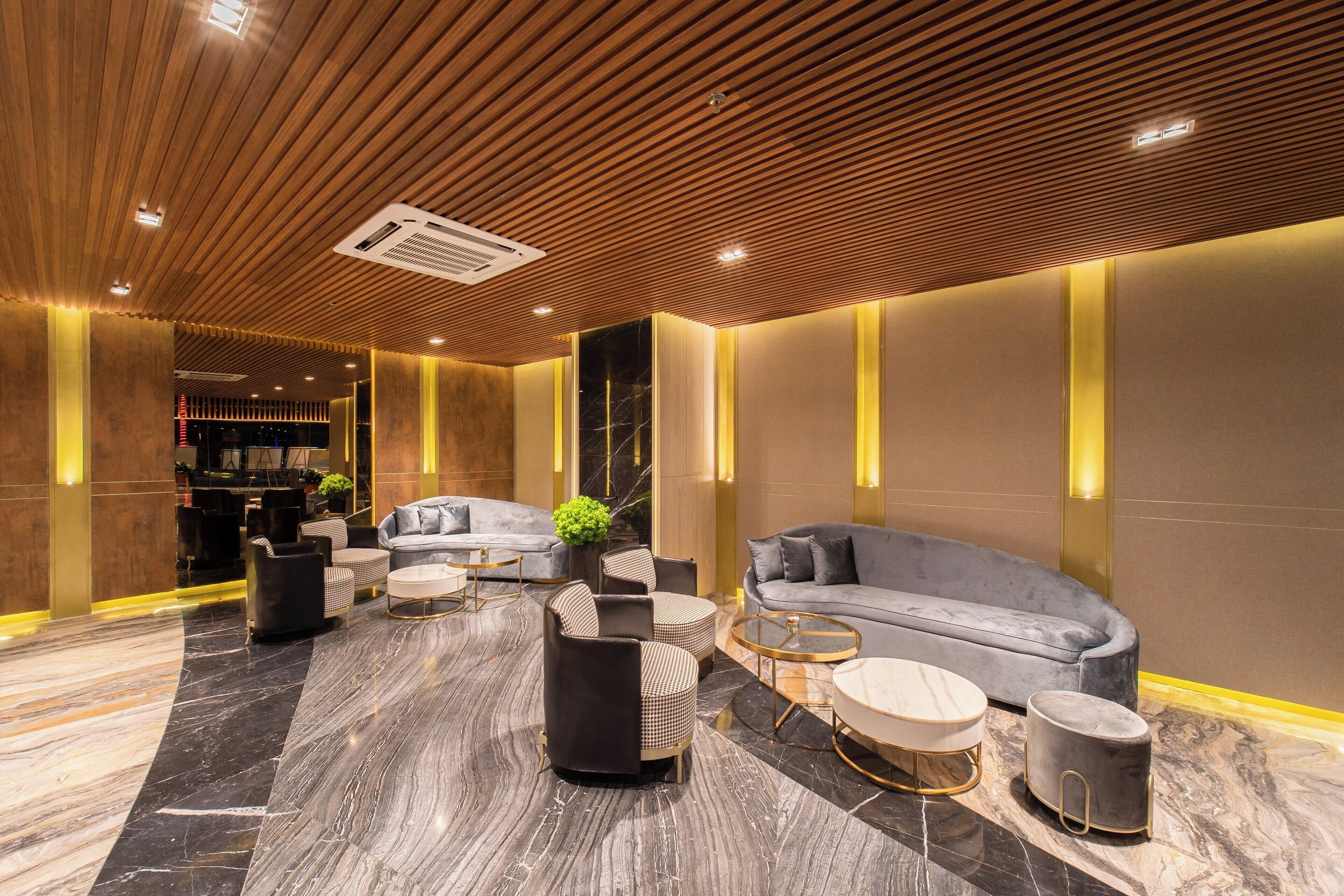 Um lobby moderno com um sofá cinza curvo, poltronas pretas e piso de mármore.