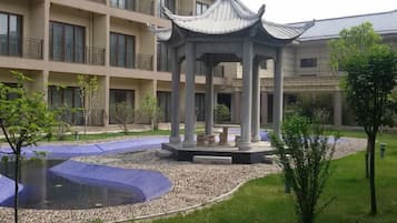 Um pátio com um pavilhão tradicional, uma piscina e um edifício com vários andares e varandas.