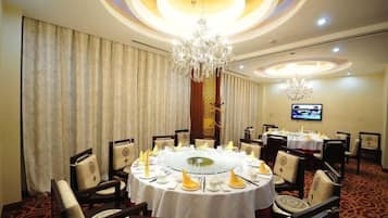 Mesa de jantar redonda com cadeiras, lustre e televisão na parede.