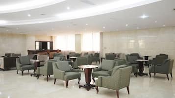 Um saguão de hotel com várias áreas de estar, uma recepção e uma grande janela que proporciona iluminação natural.