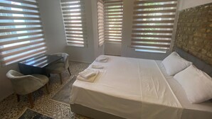 Quarto com cama, escrivaninha e duas janelas com persianas.