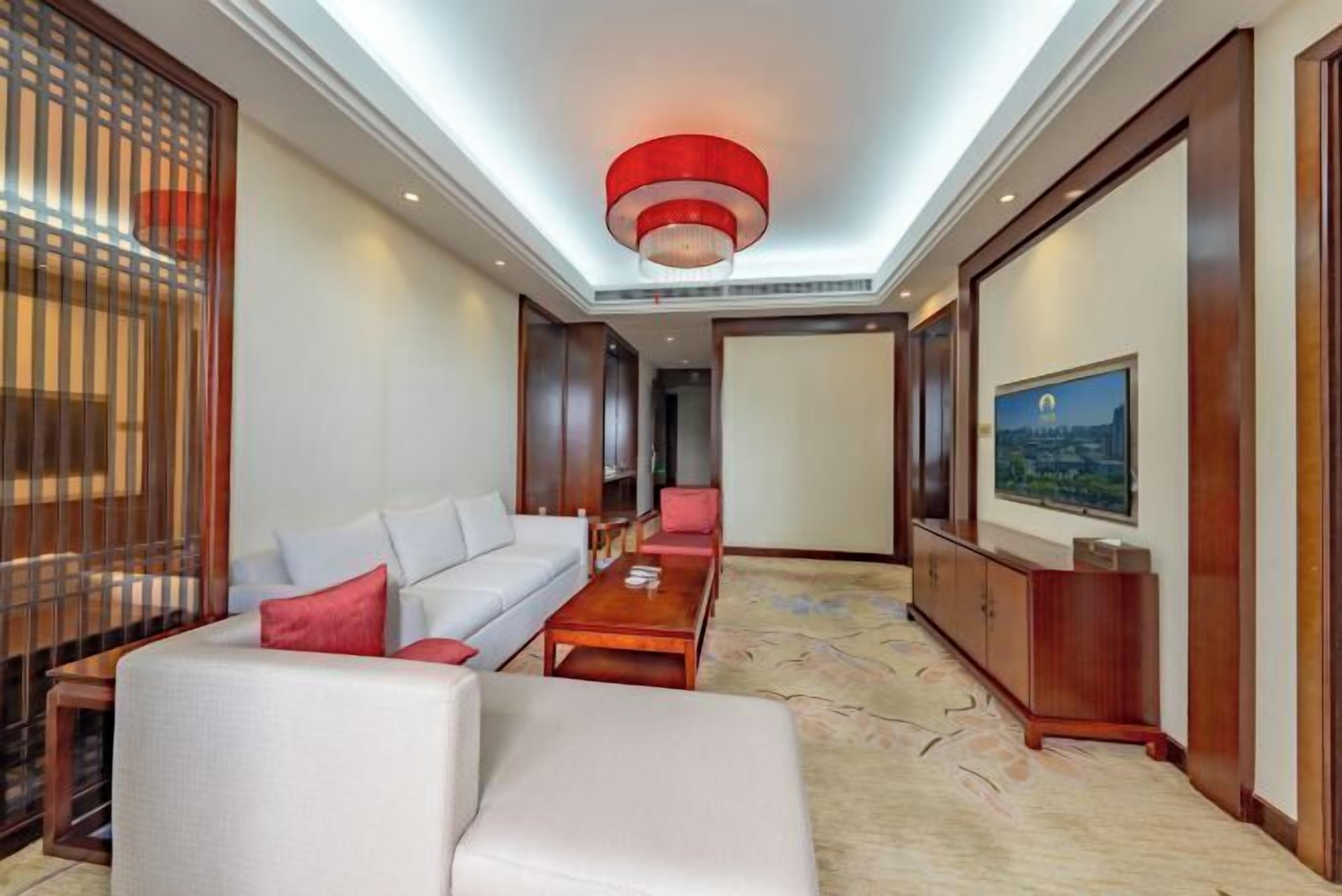 Quarto de hotel com sofá, mesa de centro, televisão e um separador decorativo.