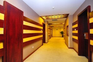 Corredor de hotel com painéis de madeira, piso carpetado e luminária no teto.