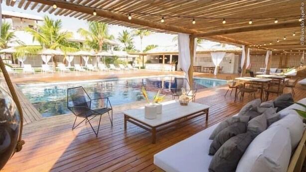 Um deck de madeira com piscina, cadeiras de sol e área de estar com almofadas.