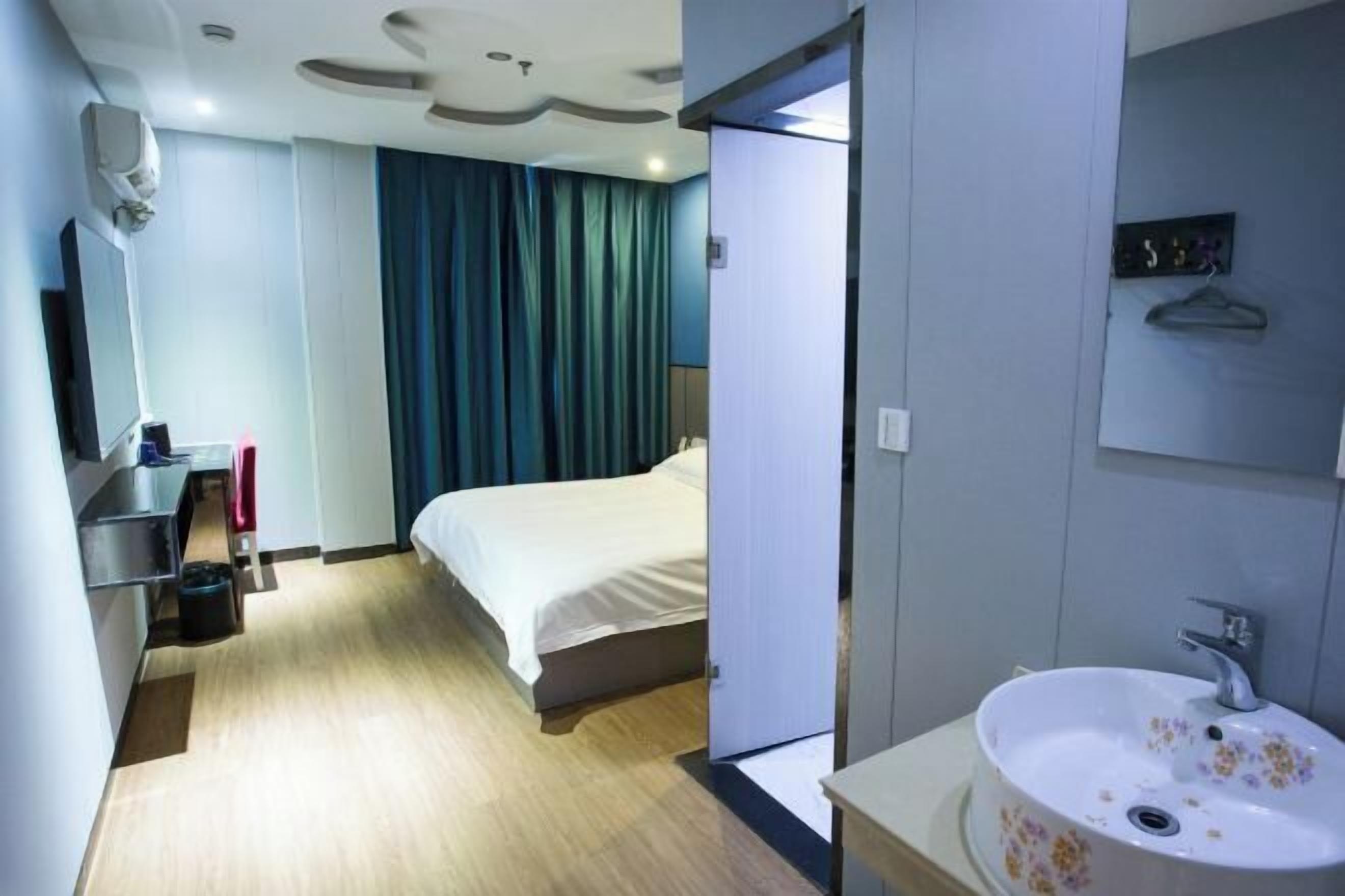 Quarto de hotel com uma cama, banheiro com pia e espelho, e uma televisão na parede à esquerda.